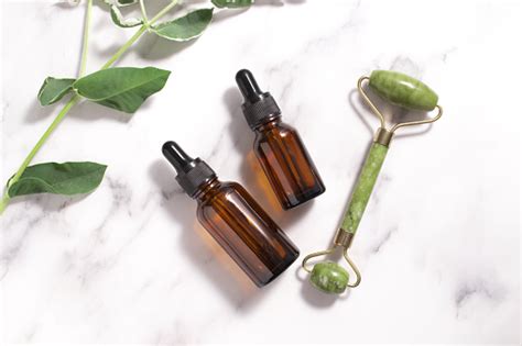 브랜드가없는 세럼 병 대리석 배경에 나뭇잎이있는 얼굴 롤러 얼굴 마사지 치료를위한 비취 얼굴 롤러 안티 에이지 리프팅 및 토닝 처리 개념에 대한 스톡 사진 및 기타 이미지