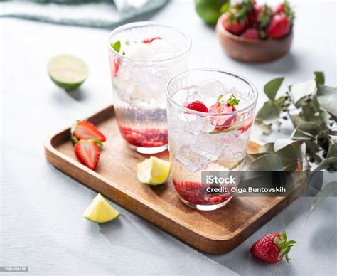 신선한 딸기 모히토는 밝은 배경에 나무 접시에 딸기 라임 민트 얼음이 담긴 유리에 담겨 있습니다 파티를 위한 여름 상쾌한 음료의