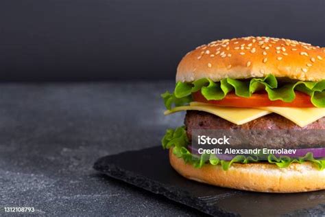 수분이 많은 고기 토마토 양파 치즈 샐러드를 곁들인 신선한 맛있는 수제 버거가 나무 판에 복사 공간을 갖춘 어두운 돌 배경에 있습니다 측면 보기입니다 패스트 푸드 클로즈업