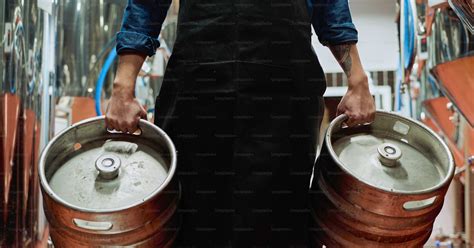 앞치마를 입은 맥주 생산 공장의 남성 노동자가 거대한 강철 탱크의 줄을 따라 카메라 앞에서 움직이면서 두 개의 수조를 들고 있다