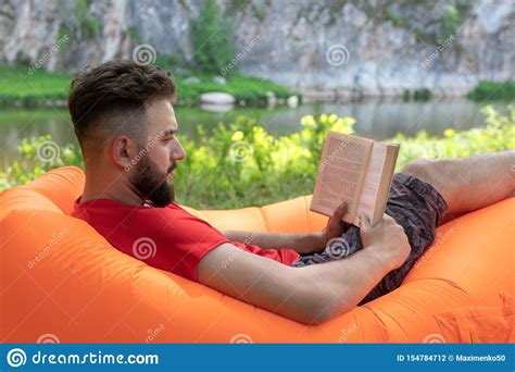 Bearded Man Or Guy Is Reading A Book Lying On The Orange Inflatable Air
