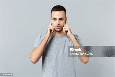 스튜디오에서 회색 벽 배경에 고립 된 손가락으로 귀를 덮고 카메라를 찾고 캐주얼에 관심 젊은 남자의 초상화 사람들은 진심으로 감정 라이프 스타일 개념입니다 복사 공간을 모의