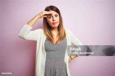 분홍색 고립 된 배경 위에 서있는 젊은 아름다운 여성은 이마에 손을 대고 걱정하고 위기에 대한 불안에 대해 강조했습니다 갈색
