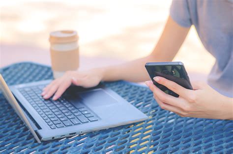 야외 자연 공원의 테이블에 노트북과 함께 손에 스마트 폰과 커피 컵을 사용 하 여 여자 손 기술 비즈니스 및 프리랜서 작업 개념입니다 전화에 초점 노트북에 대한 스톡 사진