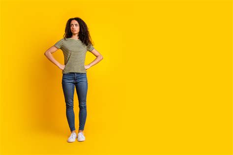 허리에 팔을 들고 진지한 소녀 옷을 입은 줄무늬 티셔츠의 전체 크기 사진은 생생한 노란색 배경에 고립 된 빈 공간을 보입니다 18 19세에 대한 스톡 사진 및 기타 이미지