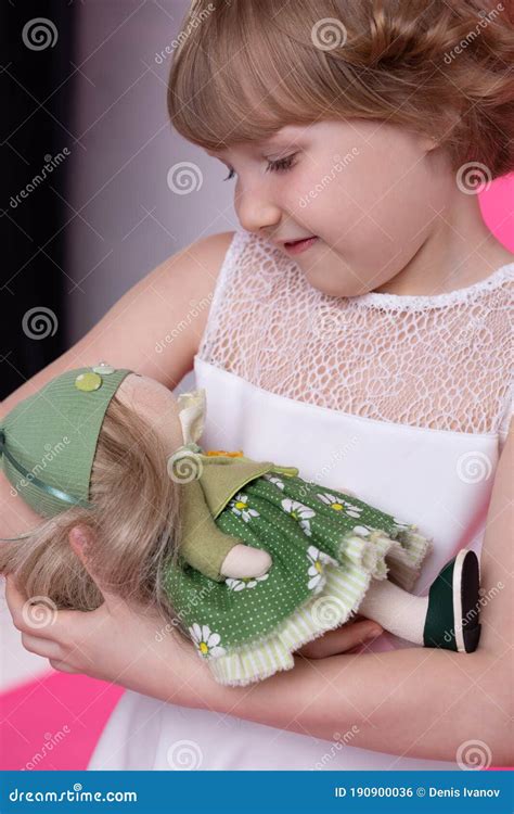 Una Bambina Felice Tiene In Braccio Dolcemente La Sua Bambola Preferita Con Un Cappello Verde E