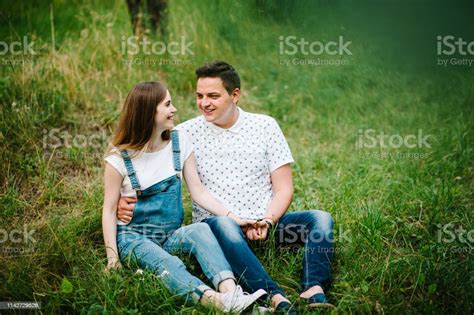 임신 한 여자와 그녀의 남편은 포옹 행복 뱃속에 손을 잡고 정원 배경에서 야외에서 잔디에 앉아 닫습니다 전체 길이 서로 봐 2