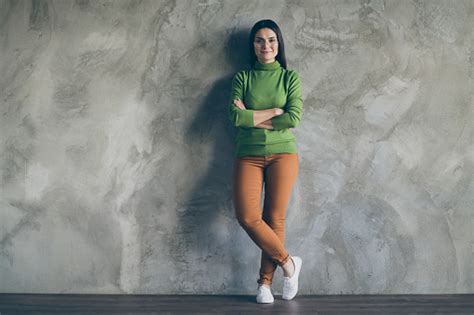 전체 길이 바디 사이즈 사진 의 쾌활 한 긍정적 인 귀여운 예쁜 예쁜 여자 서 자신있게 서 다리 를 입고 안경을 착용 하는 벽 콘크리트 회색 색상 배경 갈색 머리에 대한