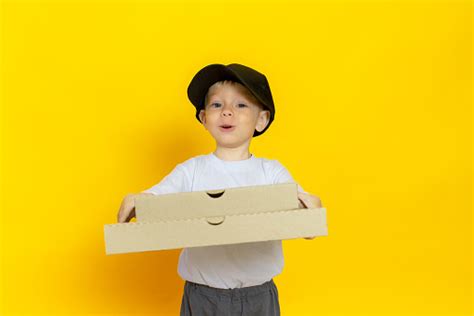 피자 배달 소년 개념 아이는 얼굴에 즐거운 표정으로 피자 두 상자를 제공합니다 검은 색 모자와 흰색 티셔츠를 입은 노란색 배경에 서 있습니다 2 3 살에 대한 스톡 사진 및