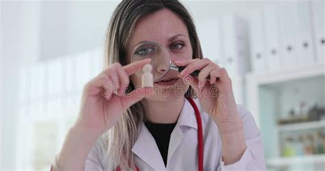 Female Doctor Examines Small Figure Using Magnifying Glass In Medical