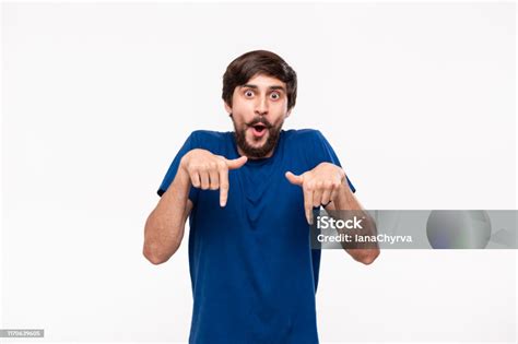 수염과 콧수염이 있는 파란색 셔츠를 입은 잘생긴 브루넷 남자가 흰 배경 위에 고립된 서 있는 손가락으로 가리킵니다 제품 및 광고의 장소 T 셔츠에 대한 스톡 사진 및 기타