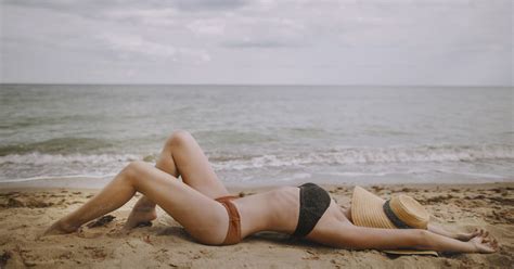 해변에 누워 모자를 쓴 검게 그을린 소녀 밀짚모자로 덮고 있는 세련된 젊은 여성 바다 근처 모래 해변에서 휴식을 취합니다 여름 방학 및 여행 마음 챙김과 평온 사진