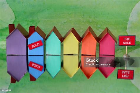 거울 표면에 반사된 다색 골판지 집의 줄 끝에 있는 For Sale 사인 이미지 파란색 모델 하우스의 판매 기호 전경에 초점 얼룩덜룩한 녹색 배경 가족 재정 부동산 및 휴가
