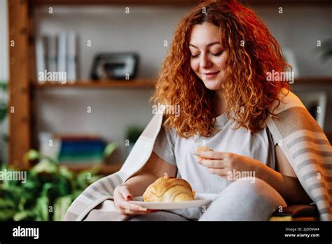A Hungry Redhead Sitting At Her Cozy Home In The Morning And Having Pastry For Breakfast Stock