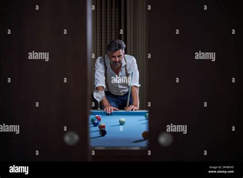 Through Doors Shot Of Positive Adult Man Leaning On Blue Pool Table With Glass Of Cocktail And