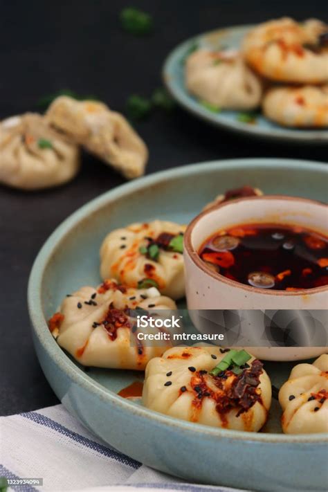 찐 모모 돼지 고기와 혼합 야채로 가득 찬 흰 밀가루와 물 반죽의 클로즈업 이미지 칠리 오일 디핑 소스의 라메킨을 둘러싼 요리에 칠리 오일을 뿌린 검은 표면 전경에 초점 0