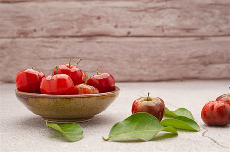 잘 익은 붉은 아세로라 체리는 세라믹 그릇에 담긴 과일과 나무 벽 배경의 시멘트 바닥에 녹색 잎을 남긴다 0명에 대한 스톡 사진 및 기타 이미지 Istock