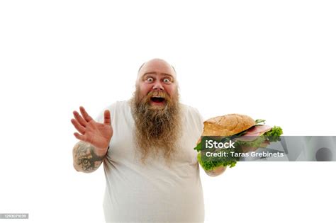 문신을 한 팔을 들고 수염을 기리는 뚱뚱한 남자가 큰 햄버거를 손에 들고 기뻐했습니다 건강에 해로운 식습관 가공육에 대한 스톡 사진 및 기타 이미지 Istock