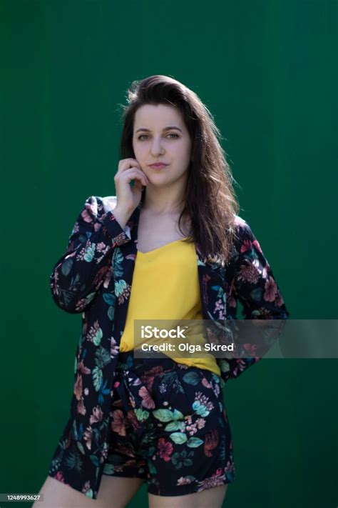 매력적인 젊은 갈색 머리 여자 에 노란색 티셔츠와 꽃 반바지 의상 녹색 벽 배경 복사 공간을 복사합니다 20 29세에 대한 스톡