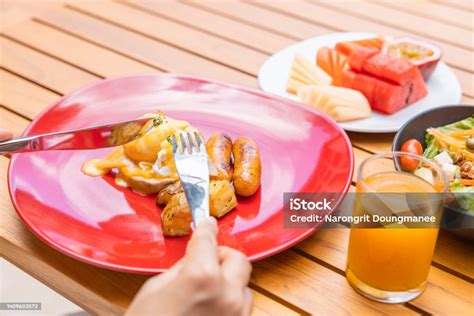 포크를 들고 아침 식사를 먹는 여자의 손 계란 베네딕트 수박 파파야 멜론 열정 과일 오렌지 주스 및 커피와 같은 과일 회색