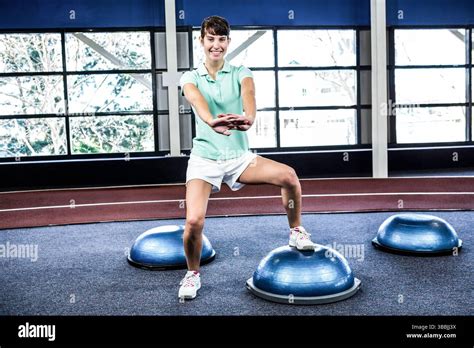 Adult Woman Performing Squat On Blue Bosu Trainer In Gym Studio Near