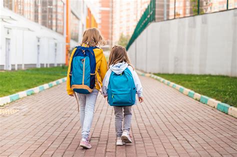 초등학교 초등학교로 돌아 가기 어린 소녀들 큰 배낭을 가진 자매들은 가을 아침에 혼자 일학년에 늦게까지 서둘러 간다 교육 아이들의 미래 행복하고 불행한 학생 아이들은 스스로