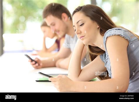 Side View Of Three Bad Students Distracted Using Smart Phones During A