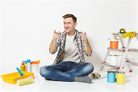 캐주얼 옷 흰색 배경에 고립 된 재건축 아파트 룸에 대 한 악기와 함께 바닥에 앉아에서 웃는 행복 한 남자 벽지 액세서리를 붙이기 그림 도구 수리 가정 개념입니다 개선에