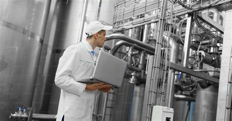 흰 코트를 입은 기술자가 공장에서 노트북에 필요한 항목을 작성합니다 생산 공장에서 노트북으로 작업합니다 노트북 컴퓨터를 손에 든 엔지니어는 파이프 라인의 장치를