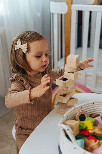 놀이방의 테이블에 나무 블록을 가지고 노는 어린 소녀 현대 보육원에서 아기와 유아를위한 교육 게임 아이는 나무 무지개 쌓기 블록으로 타워를 만듭니다 2 3 살에 대한 스톡