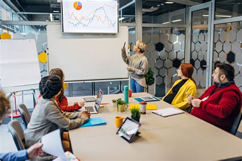 비즈니스 여성이 사무실에서 동료에게 프레젠테이션을 하고 장치 화면에 회사의 성공 그래프를 보여줍니다 모임에 대한 스톡 사진 및