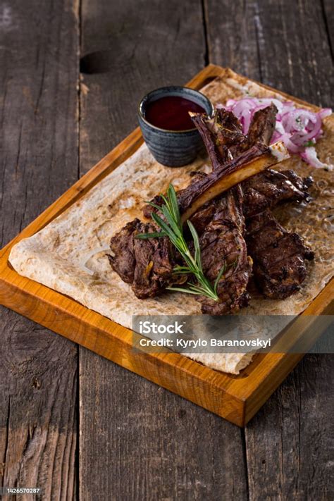 피타 빵에 절인 양파 로즈마리와 크랜베리 소스의 스프릭을 곁들인 양고기 랙 음식은 나무 판자 위에 놓여 있습니다 보드는 나무 배경에 서 있습니다 0명에 대한 스톡 사진 및