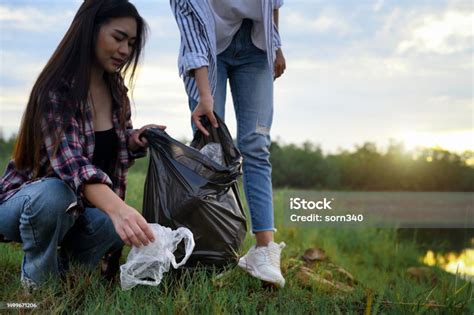 비닐 쓰레기 봉투를 들고 있는 손의 근접 촬영 두 명의 여성 자원봉사자가 자연공원에서 쓰레기와 비닐봉투를 쓰레기봉투에 수거하고