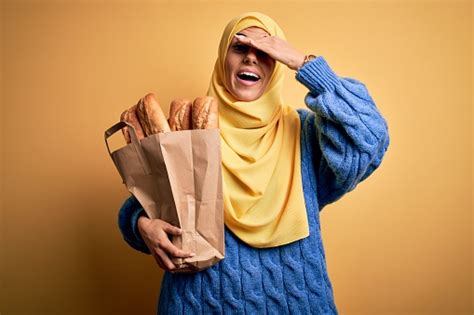 젊은 아름 다운 갈색 머리 아랍 여자 이슬람 히잡을 들고 종이 가방을 들고 빵 머리에 손으로 스트레스 수치와 깜짝 얼굴 분노와 좌절으로 충격 실수에 대한 두려움과 화가