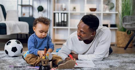 사랑하는 아프리카계 미국인 아버지와 귀여운 아들이 바닥에 함께 누워 앨범에 화려한 연필로 그림을 그립니다 집에서 가족과 함께하는 시간 공생의 개념 사진