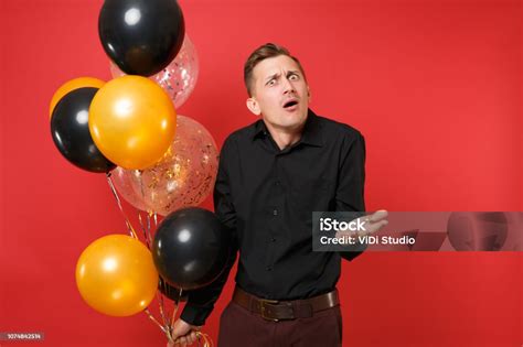 당황한 젊은이 공기 풍선 들고 검은 클래식 셔츠에 밝은 빨간색 배경에 고립 손을 확산 세인트 발렌타인 여성의 날 해피 뉴가 어 생일 이랑 휴일 파티 개념 2019년에 대한