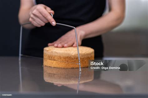 검은 앞치마를 입은 전문 과자 장수가 끈 칼로 케이크를 자르는 데 손을 얹고 있다 검은색에 대한 스톡 사진 및 기타 이미지