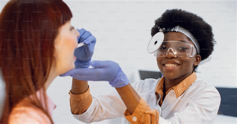 긍정적인 미소를 짓는 젊은 아프리카계 미국인 여의사 이비인후과 의사 유니폼 정면 반사경 및 안경을 착용하고 여성 환자의 목을