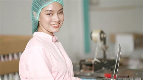 여성 영양사 또는 관리자 생산 라인 또는 감독자는 헤어넷과 멸균 의류 및 장갑을 착용하고 제조 공장 또는 공장의 생산 라인에서 태블릿으로 작업하고 웃으며 카메라를 보고