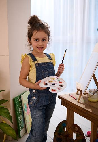 매력적인 어린 소녀 탤런트 아티스트 페인트 브러시와 팔레트를 들고 사랑스러운 아이 예술 수업을 즐기면서 나무 이젤 근처에 서 키즈 엔터테인먼트 취미 교육 창의성 4 5세에