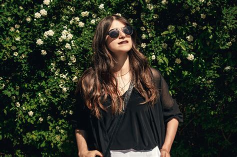 화창한 날에 꽃 덤 불에서 편안한 아름 다운 머리를 가진 아름 다운 세련 된 Hipster 소녀 정원에서 하루를 즐기고 유행 복장에 선글라스와 화려한 Boho 여자 거리에