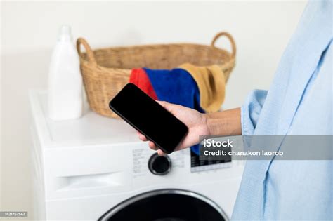 클로즈업 주부 손은 응용 프로그램과 함께 휴대 전화를 사용하여 스마트 세탁기를 작동합니다 기술 스마트 폰으로 제어되는 옷을 청소하는 여성 가사 집안일에 대한 스톡 사진 및