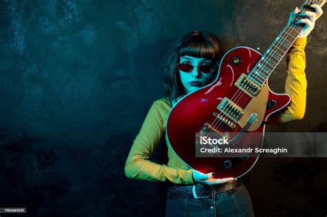 네온 불빛에 빨간 기타와 곱슬 머리를 가진 패션 젊은 소식통 여자 록 뮤지션은 일렉트릭 기타를 연주하 고 있습니다 90 년대 스타일의 개념입니다 가수에 대한 스톡 사진 및