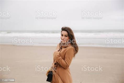 북쪽 바다 근처 해안을 따라 아름 다운 여자 걷기 잉크의 초상화입니다 바다 앞에 서 있는 유행 메이크업을 가진 브라운 코트에 있는 우아한 숙 녀 갈색에 대한 스톡 사진 및