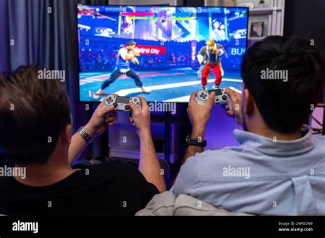 Friend Gamers Playing Video Game Of Battle Martial Arts Fighter On Tv Using Joysticks Position