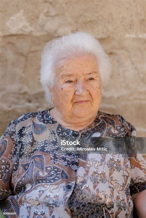 Portrait Of A Very Old Woman Seating In Front Of The Wall In A Plastic