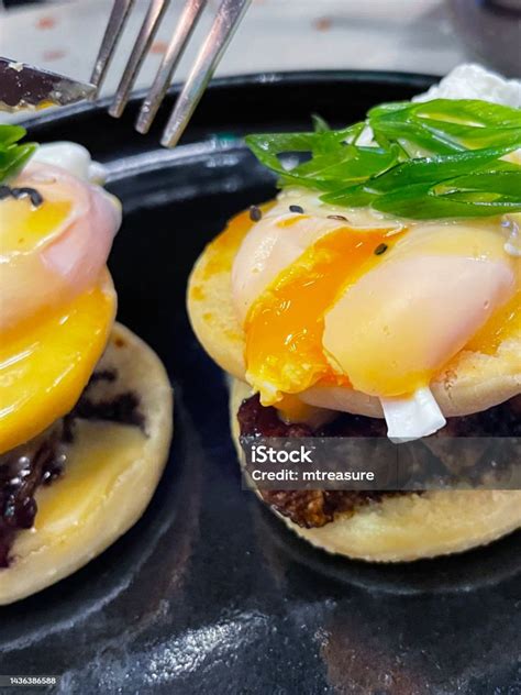 계란 베네딕트 레시피로 포크를 자르는 전체 프레임 이미지 돼지고기 소시지로 채워진 쪼개진 잉글리쉬 머핀 더미 홀랜다이즈 소스와 수란을 얹은 계란 노른자가 새어 나오는 검은