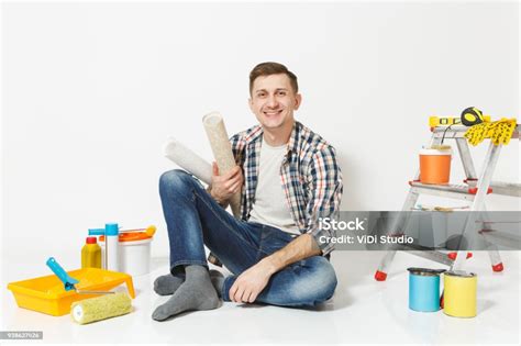 캐주얼 옷 롤 벽지 혁신 아파트 룸 흰색 배경에 고립에 대 한 악기와 함께 바닥에 앉아에서 웃는 남자 액세서리 도구 그림 붙이기 수리 가정 개념입니다 개선에 대한 스톡 사진