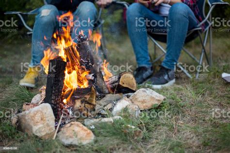 아름 다운 커플 앉아 캠프 파이어 주위에 캠핑 텐트와 배경에 남자 막대기로 화재 제스처 2명에 대한 스톡 사진 및 기타 이미지 Istock