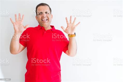 흰색 벽 위에 빨간 T 셔츠를 입고 손가락으로 10 개를 가리키는 가운데 나이 남자는 자신감을가지고 행복 하 게 웃는 다 T 셔츠에 대한 스톡 사진 및 기타 이미지 Istock